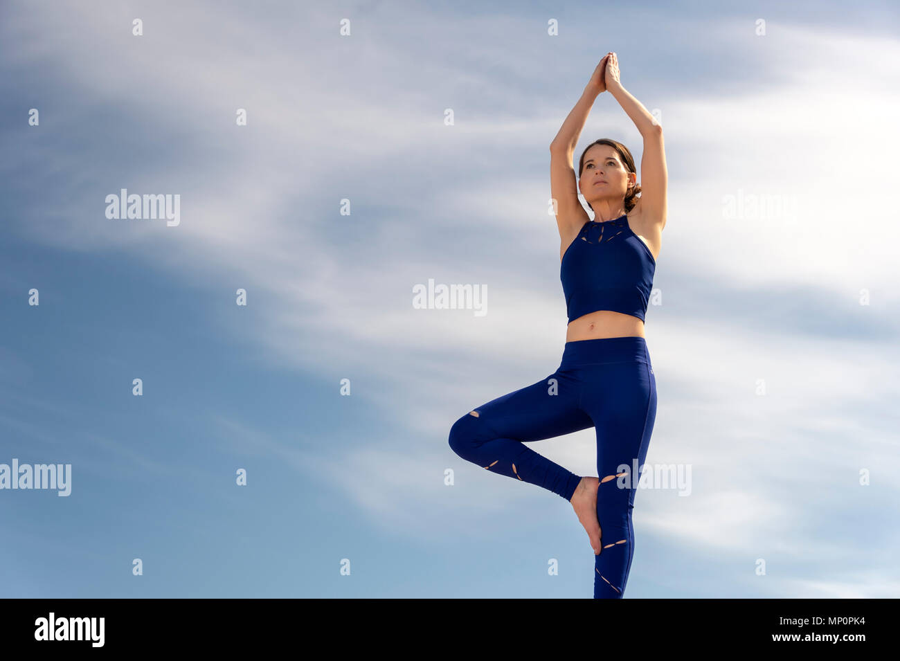 woman practicing yoga, doing a tree pose outside in the summer with a ...