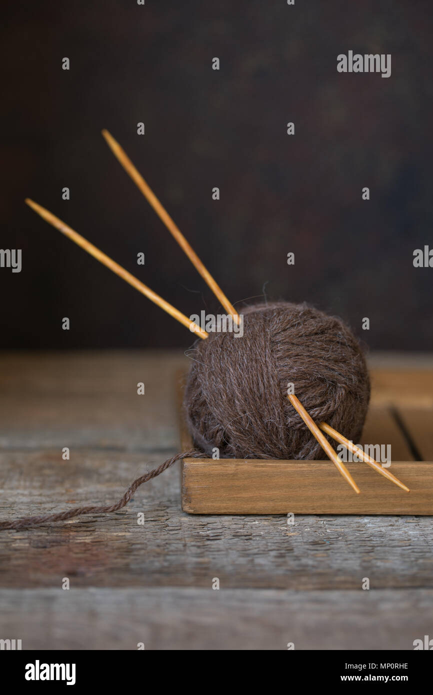 Brown yarn ball with needles on a rustic wooden background, toned, wabi ...