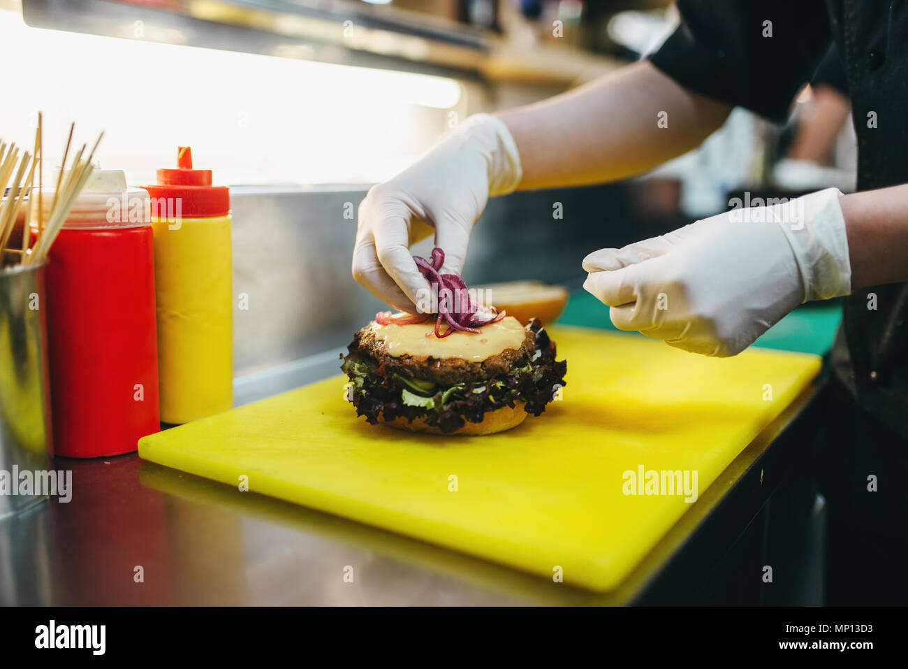 Male cook prepares fresh salad for burger. Hamburger preparation ...