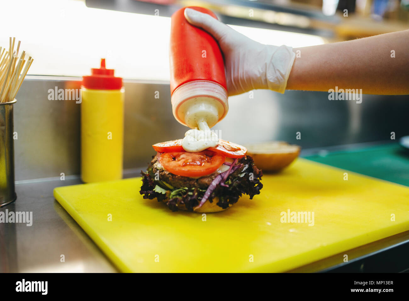 Male cook puts tomatoes in to the burger, fast food cooking. Hamburger ...