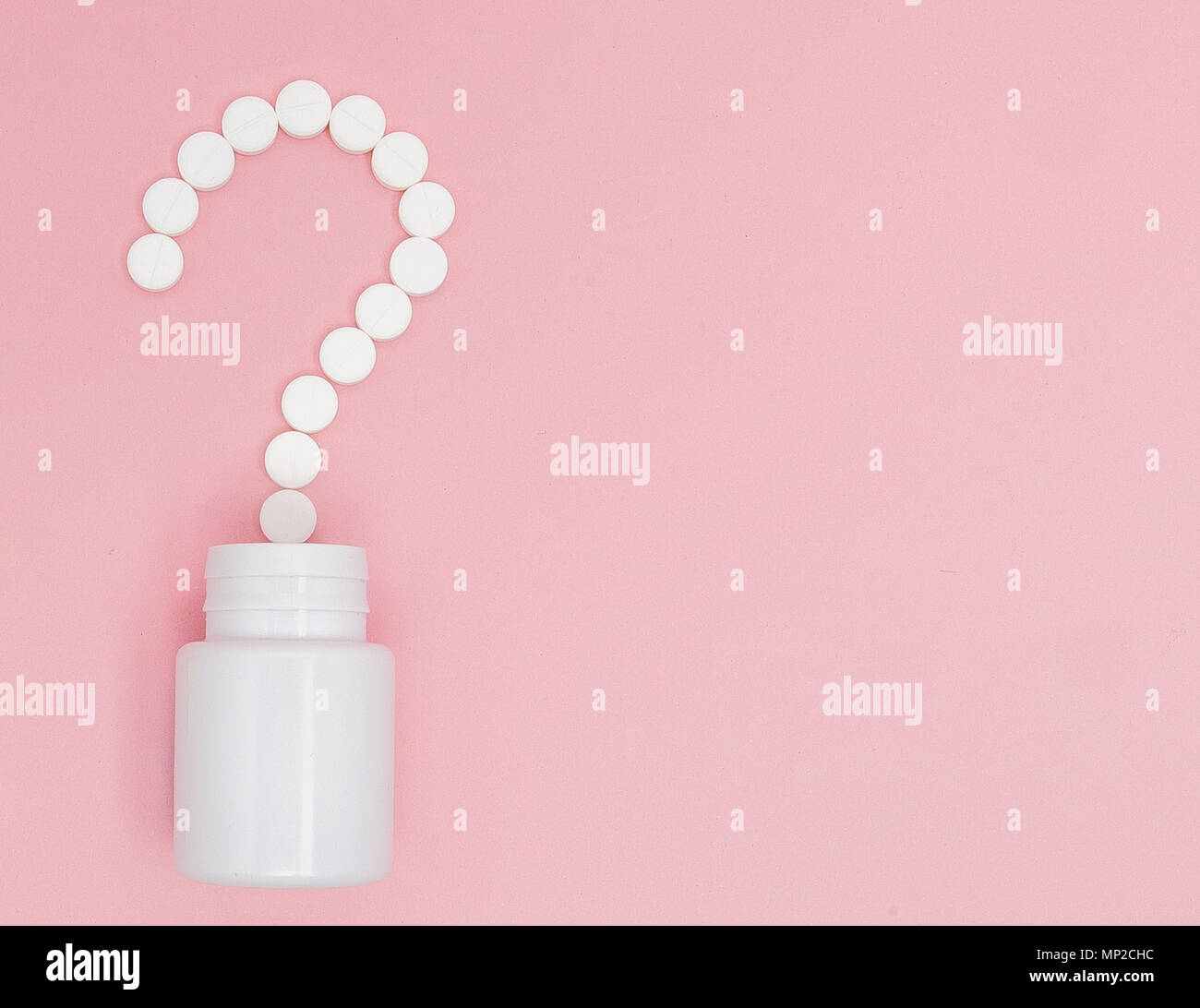A question mark, laid out of pills and a white plastic bottle on a pink ...