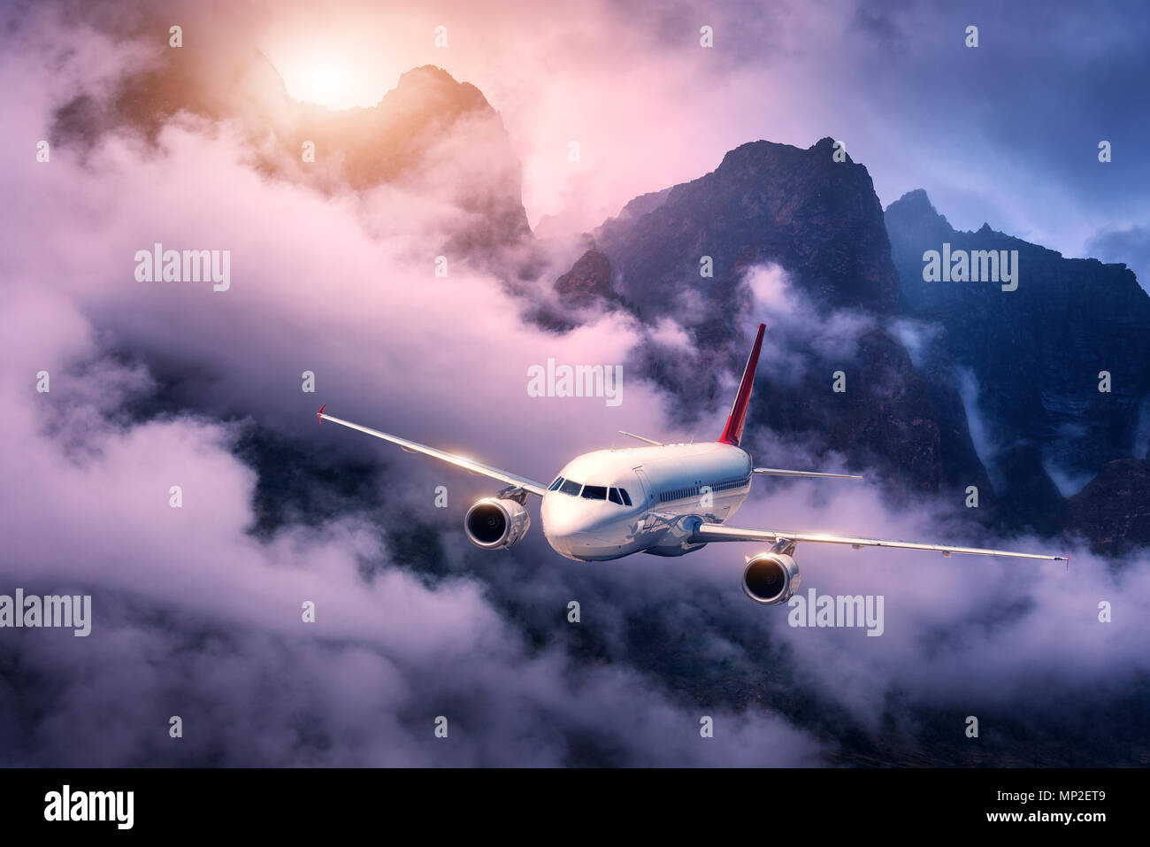 White aircraft is flying in purple clouds against high mountains at ...