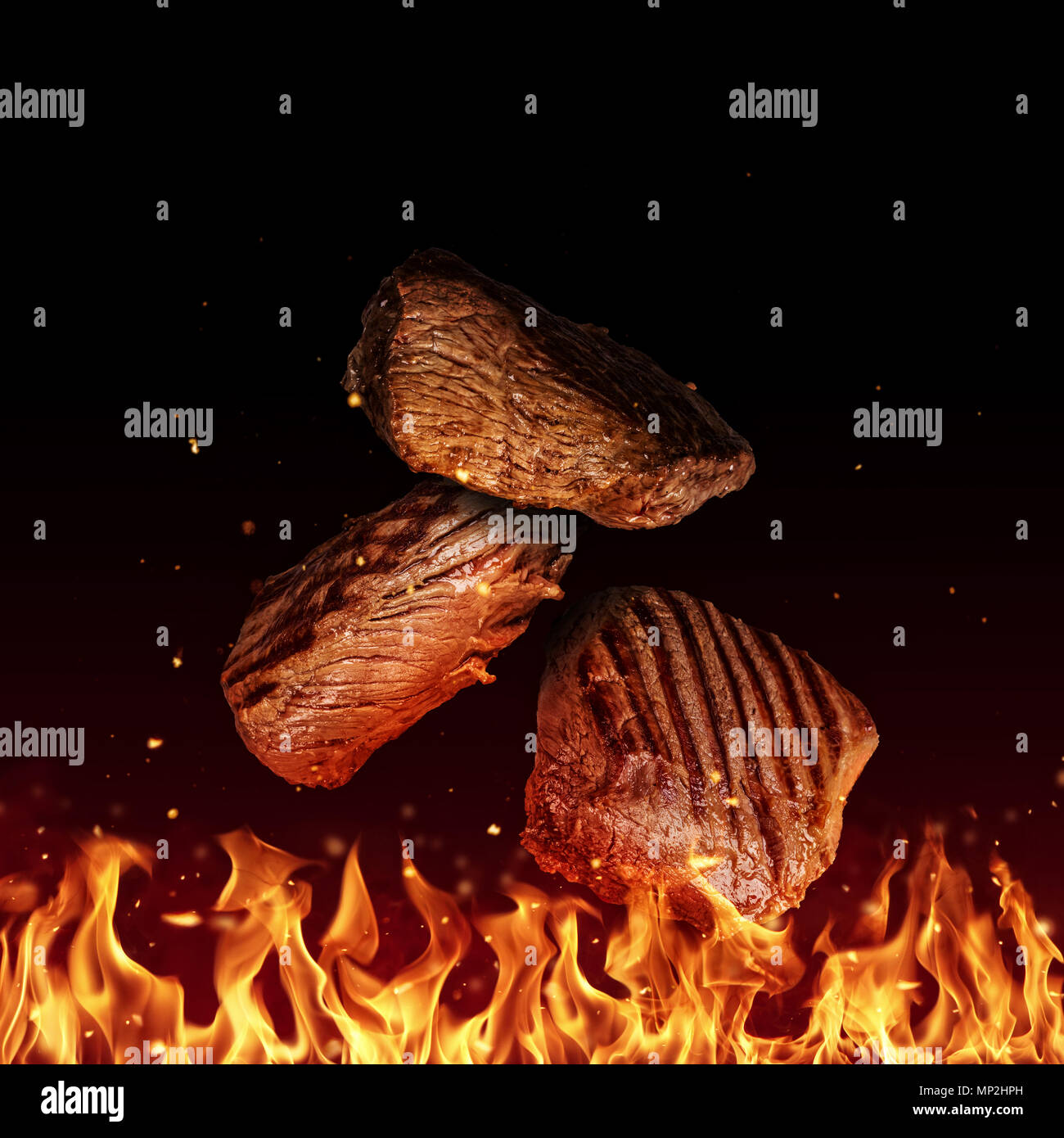 Flying pieces of beef rump steaks above grill flames, isolated on black ...