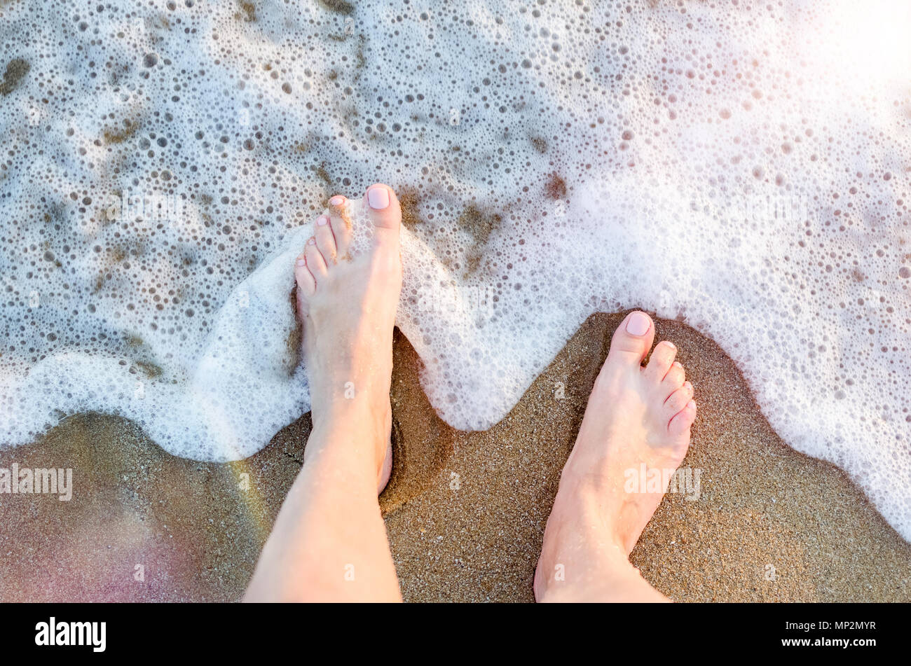 Feet of a young woman touching water on tropical beach in sunny summer ...