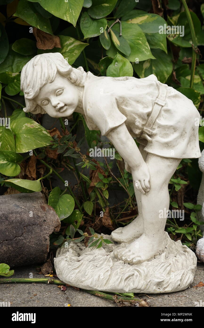 Delicate stone sculpture of a child, bending down amidst vibrant garden ...