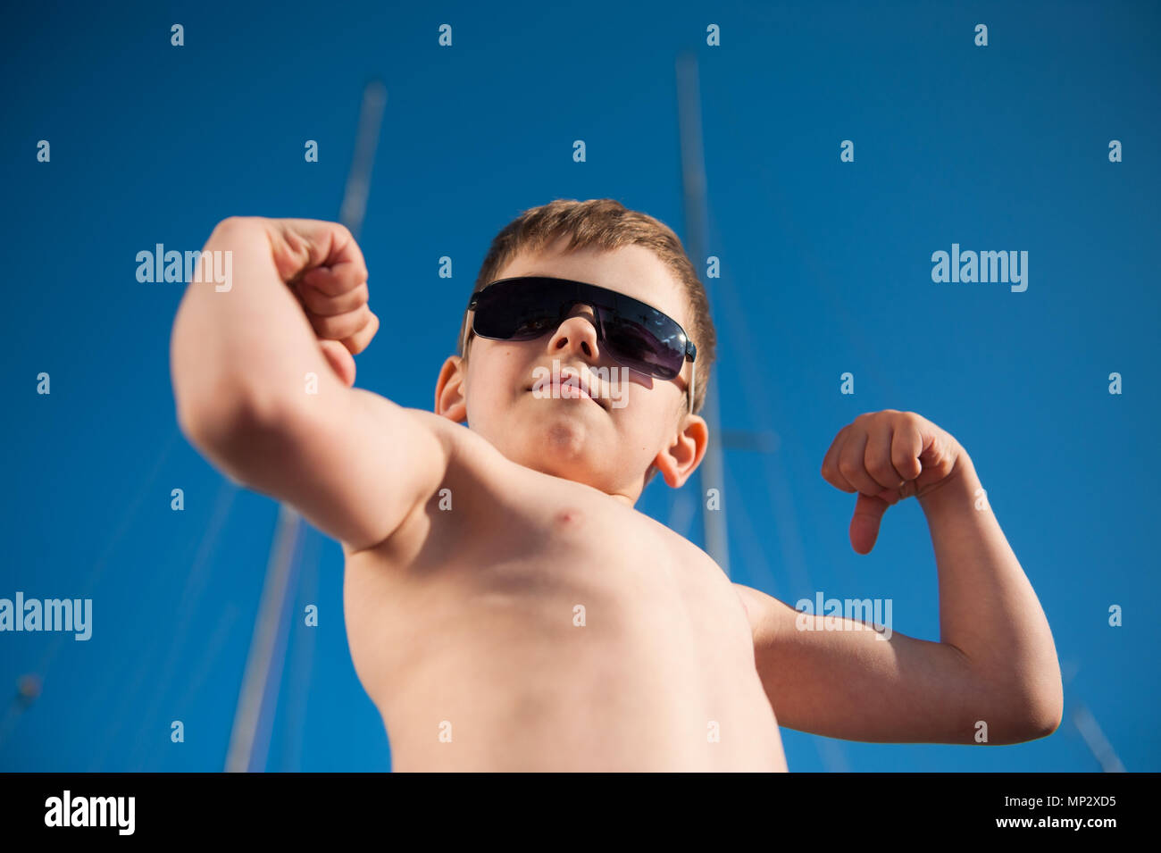 happy strong small boy wearing sunglasses showing his muscle on blue ...