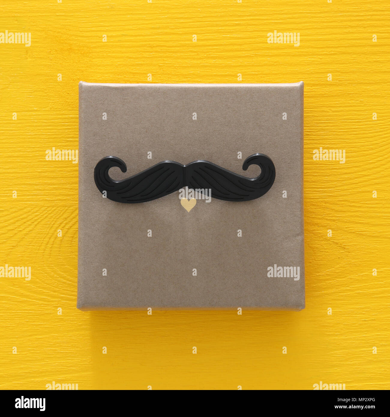 Top view of gift box with mustache over yellow wooden background ...