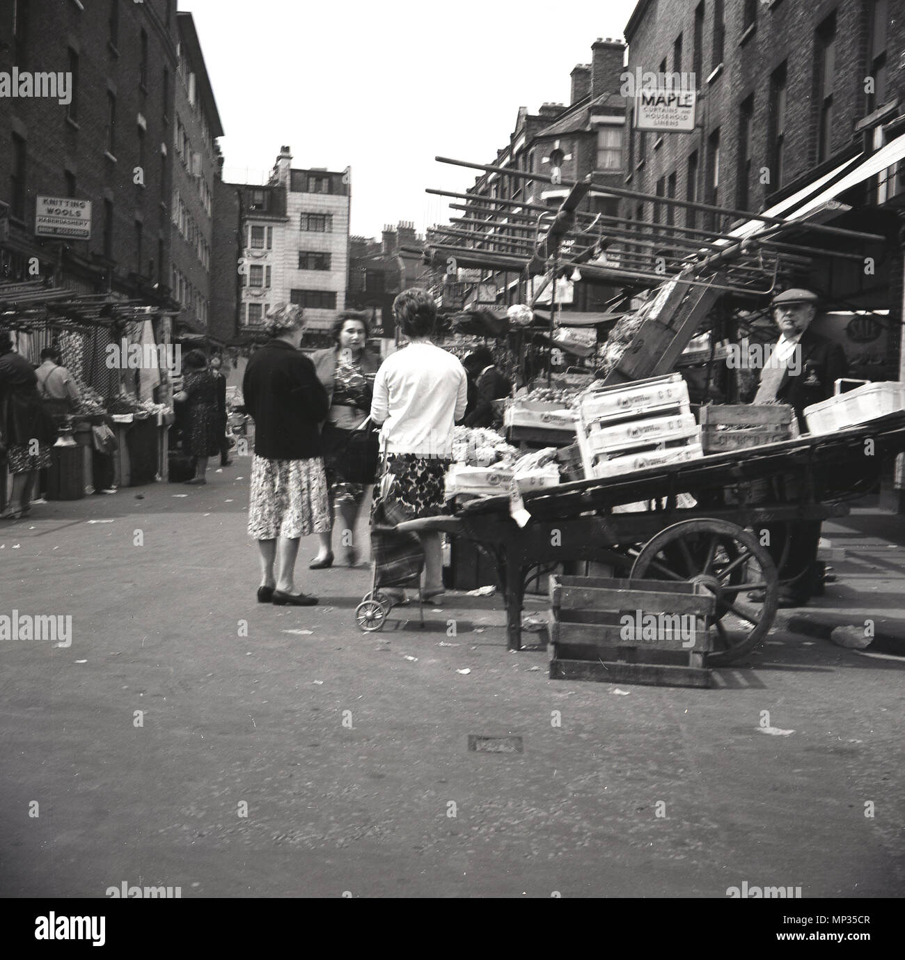 1960s, an inner city London street market with stalls, trader with cart ...
