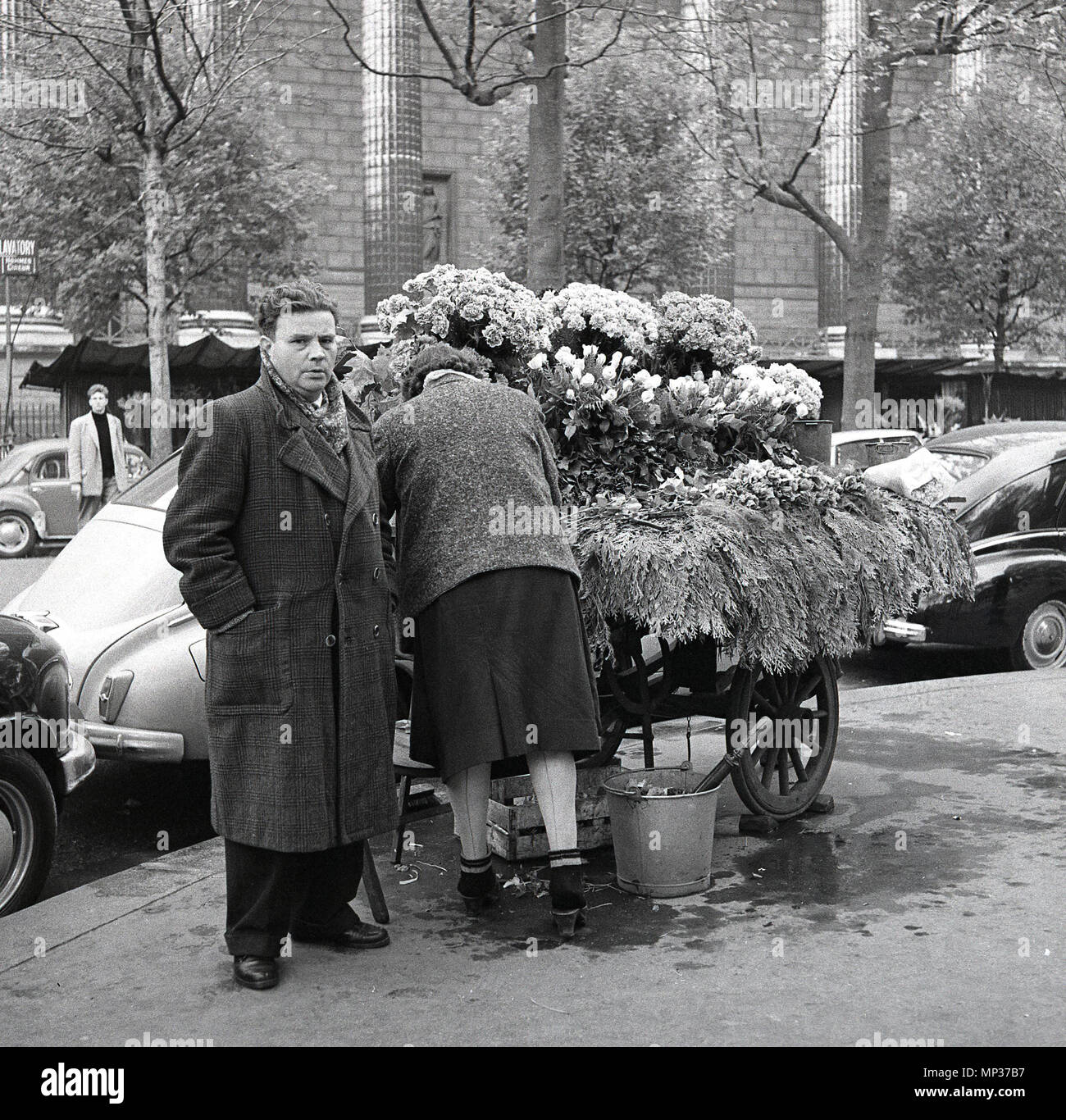 1950s, historical, a gentleman in an overcoat standing by an outdoor ...