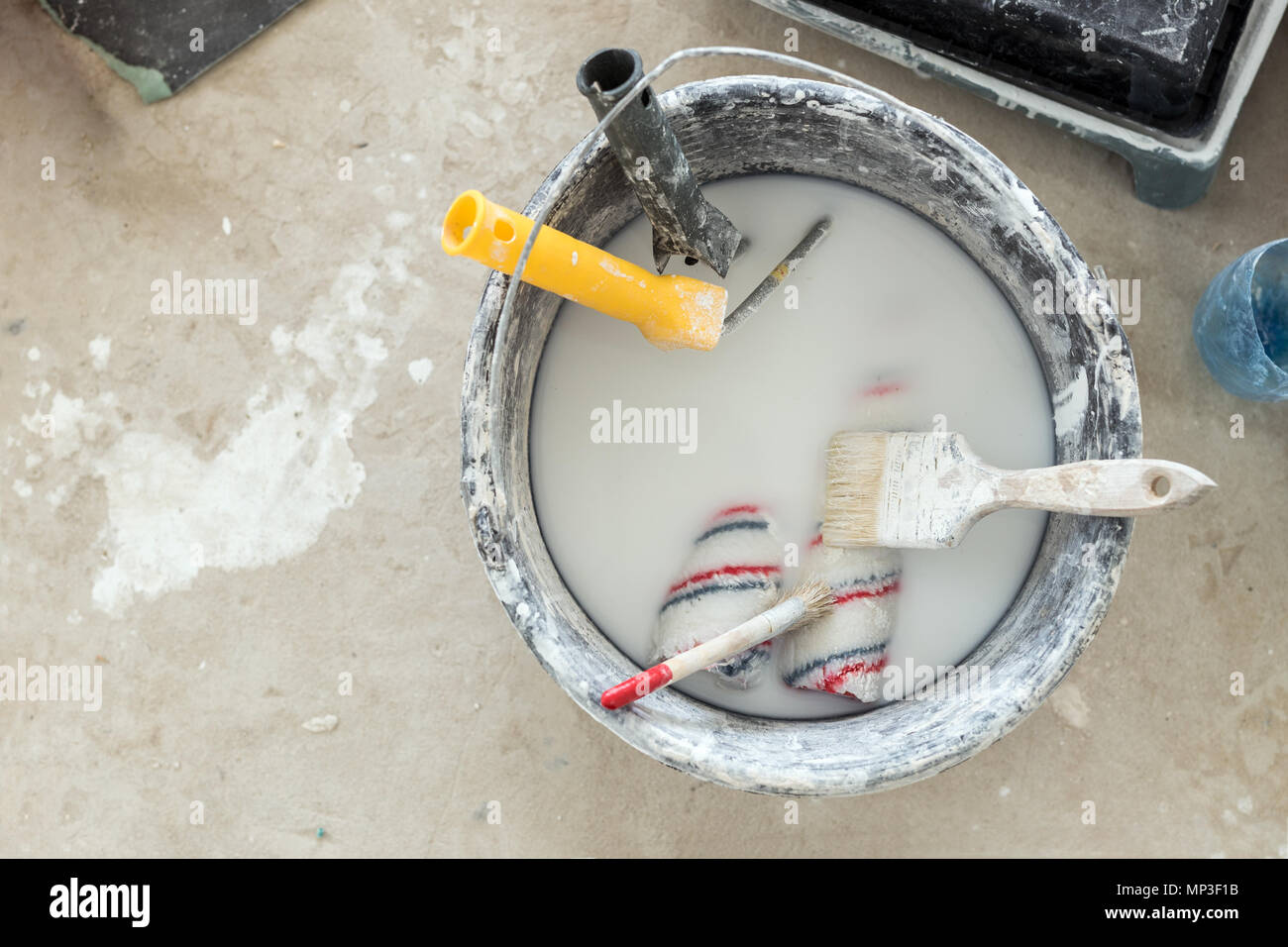 Close-up dirty bucket with used brushes and paint rollers soaked in ...