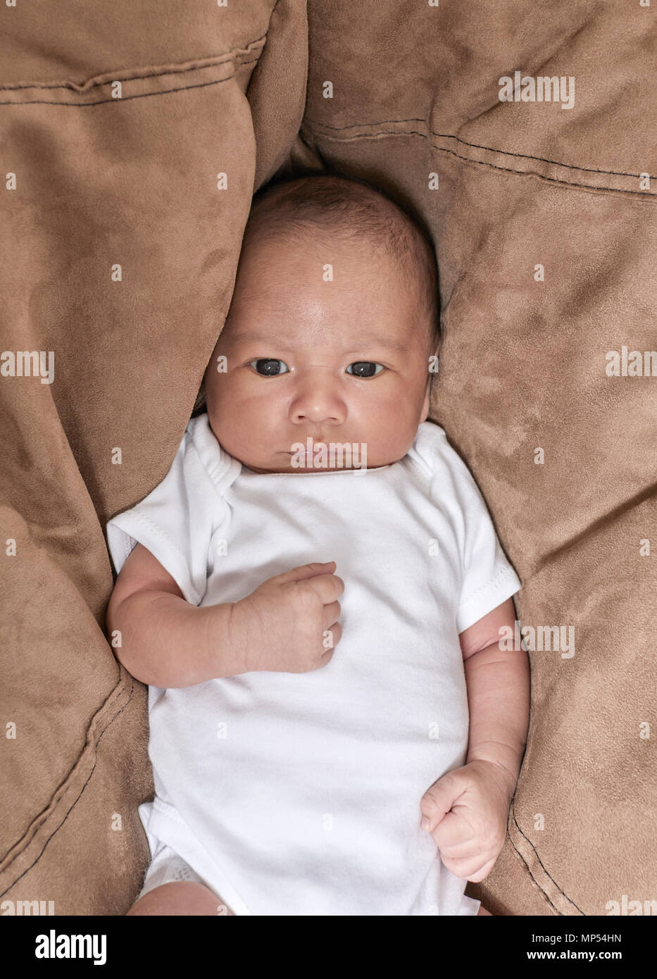 A three week old baby boy looking at the camera with his arm bent on ...