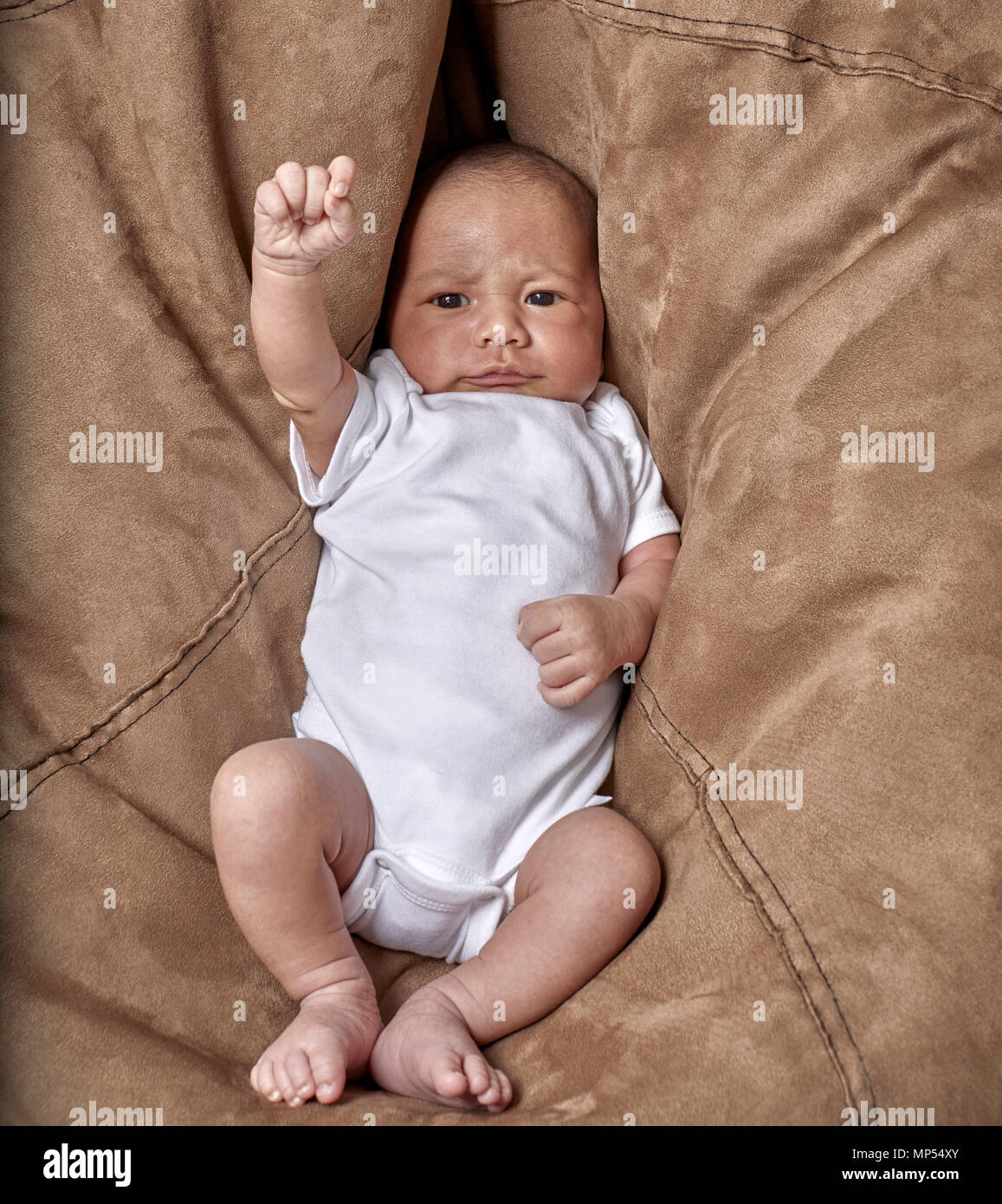 A three week old baby boy looking at the camera with his arm raised up ...