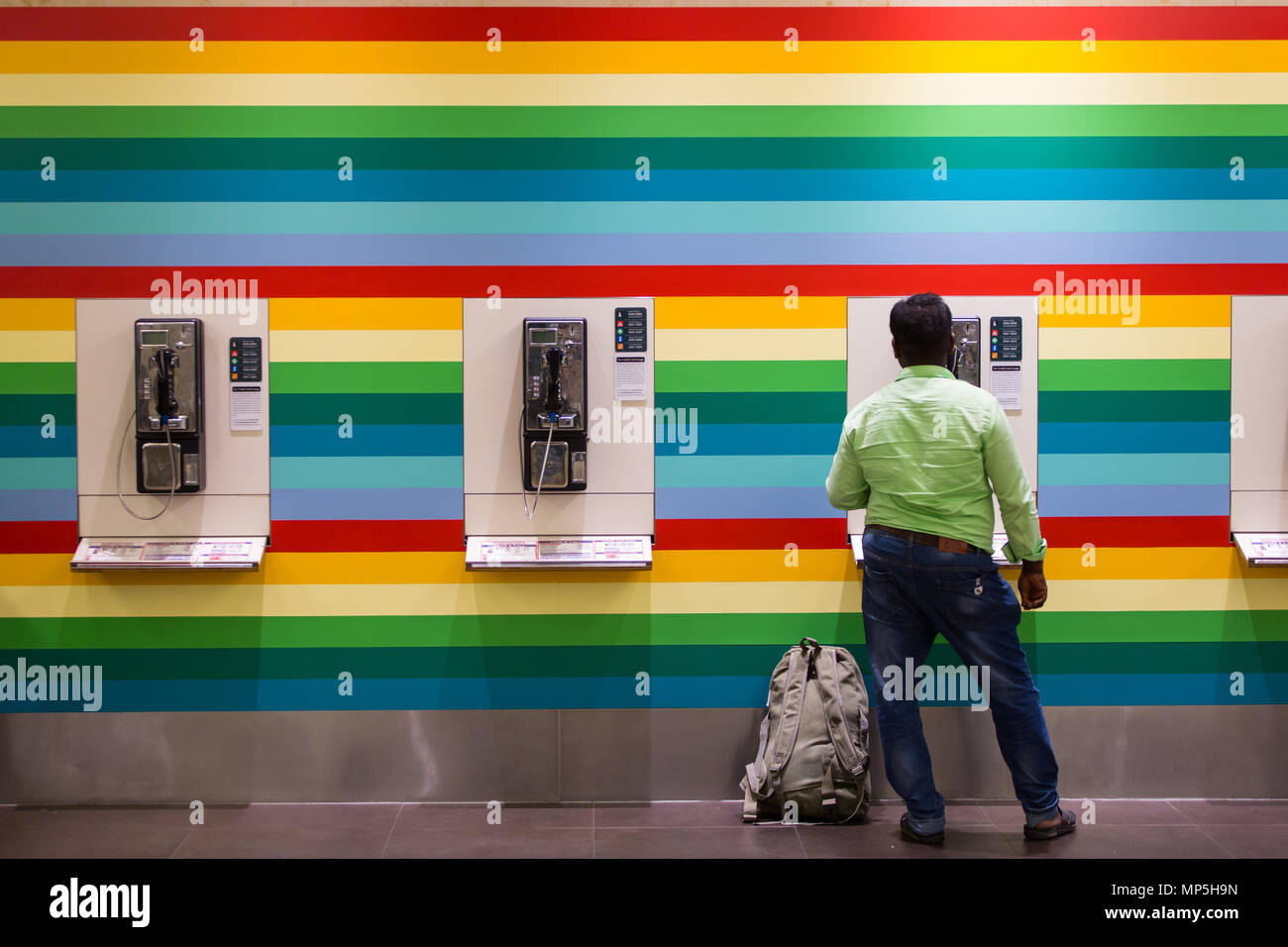 An Indian man in jeans and shirt standing at colourful stripe wall ...
