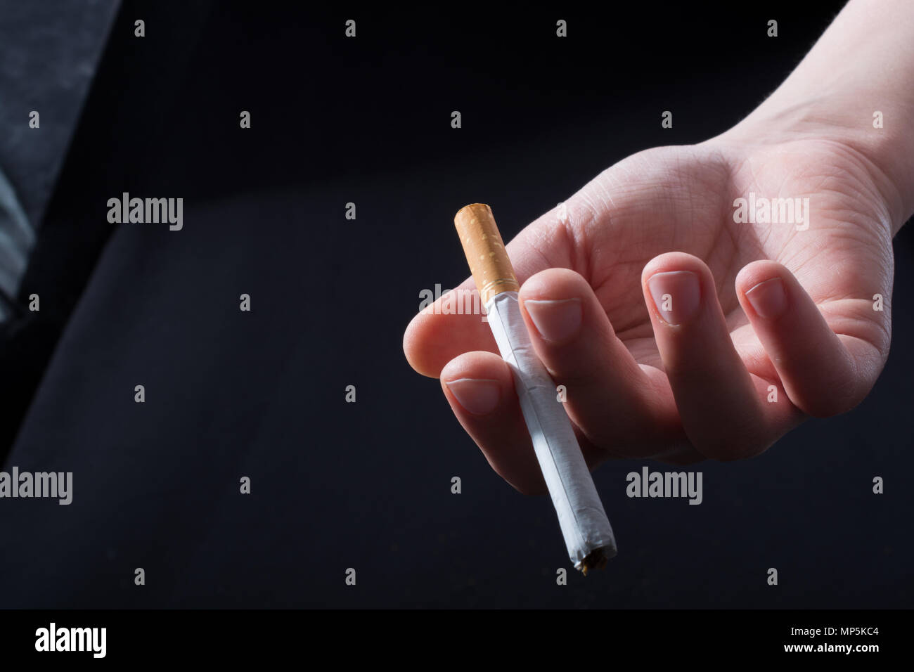 Hand is giving out cigarette on a black background Stock Photo - Alamy