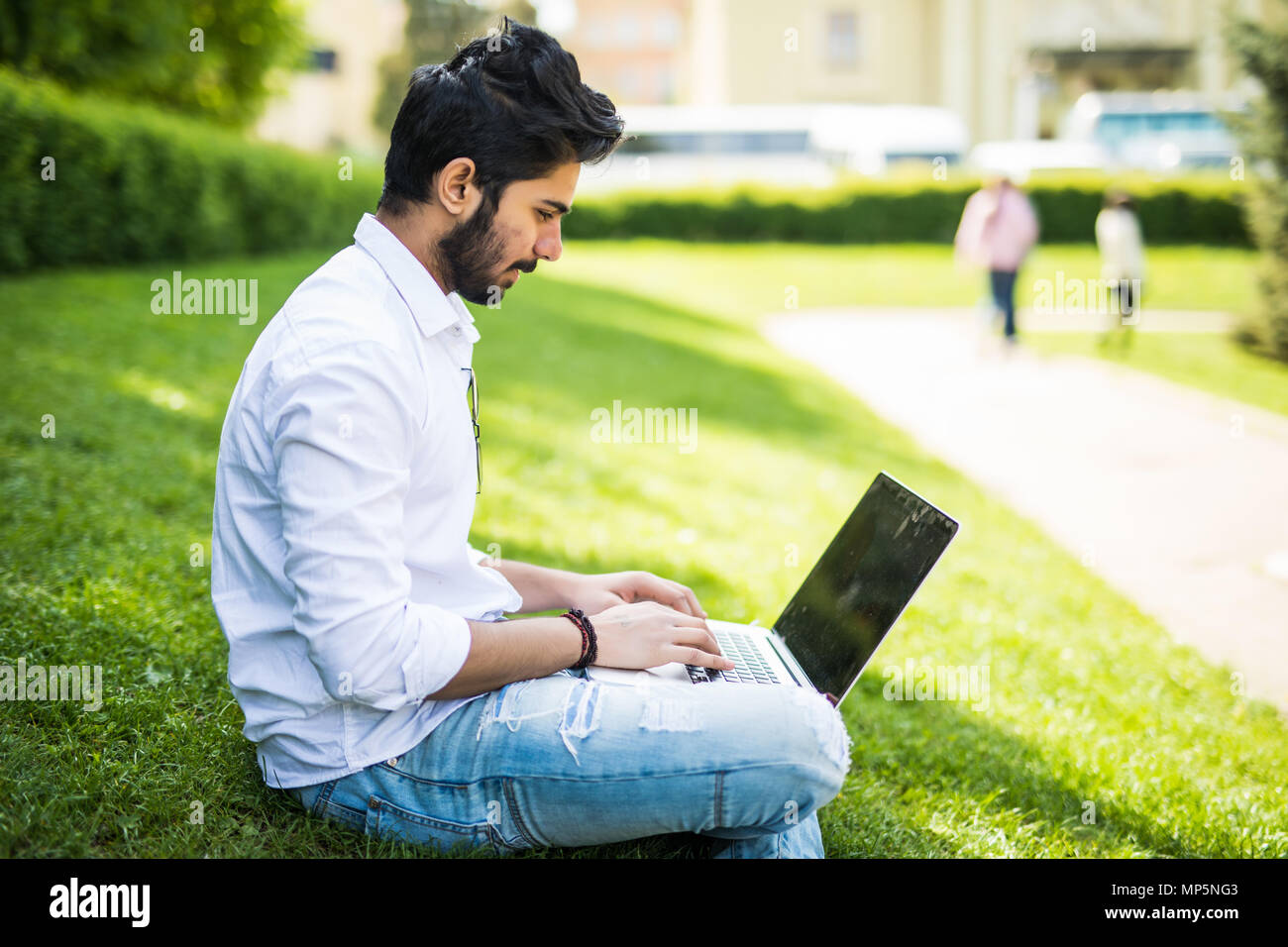 Young indian man using and typing laptop computer in summer grass Stock ...