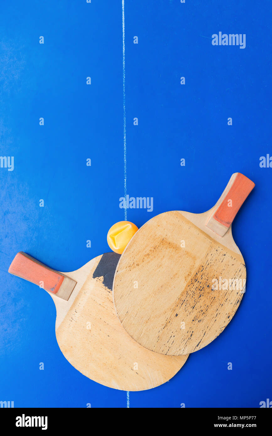 pair of old pingpong rackets and a dented ball on a blue pingpong table ...