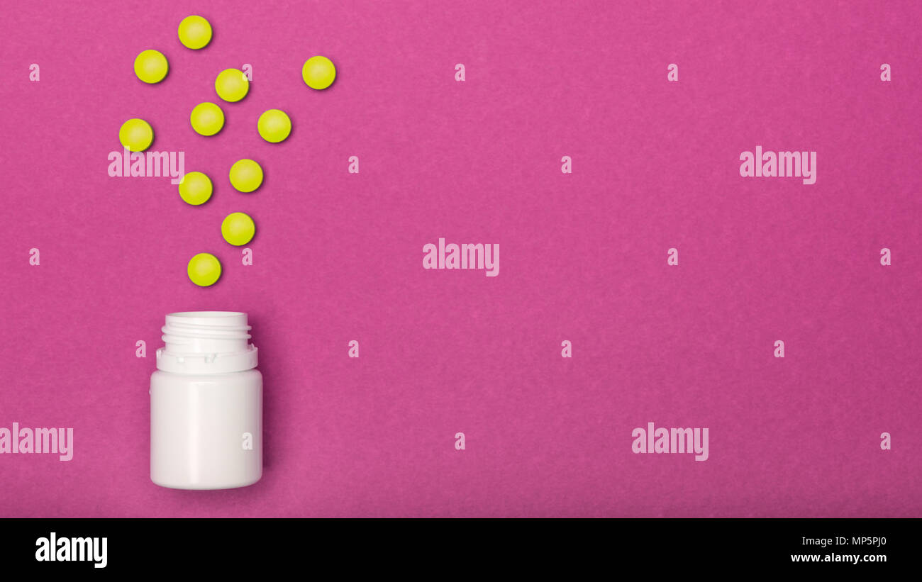 Medication bottle and yellow pills spilled on bright pink coloured ...