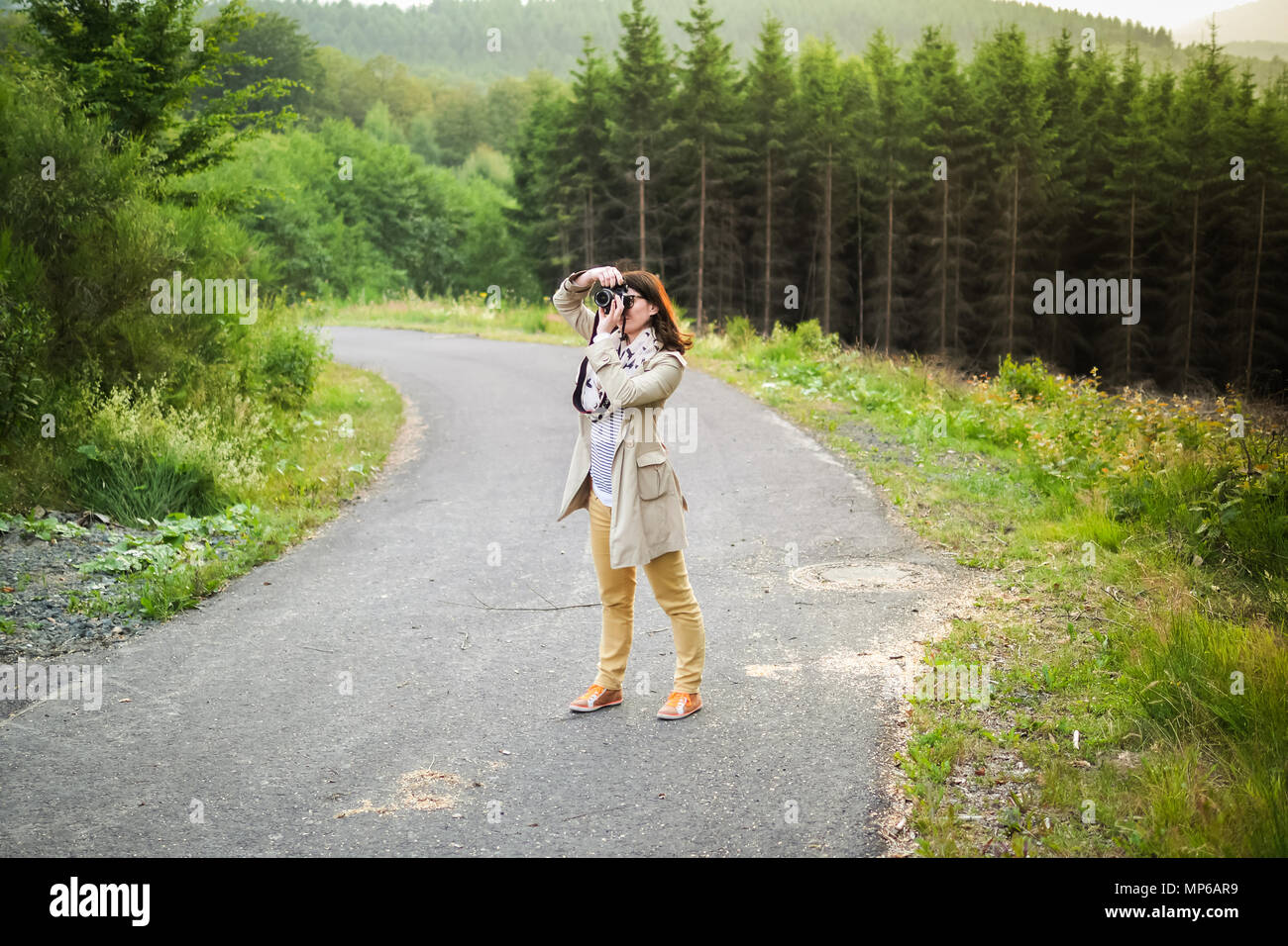 Female photographer standing on forest road taking pictures. Full body ...