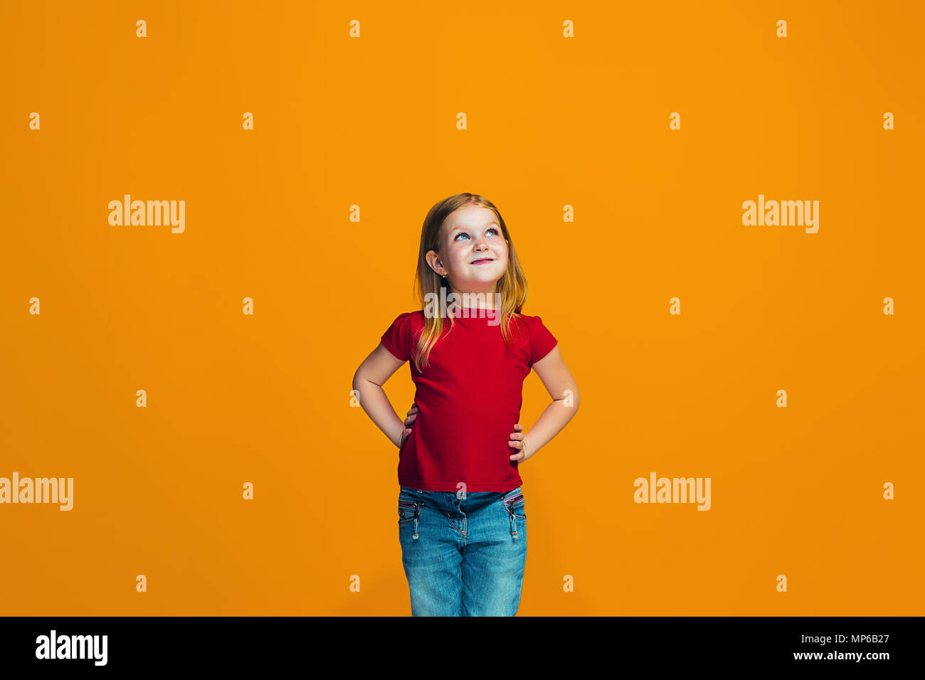 The happy teen girl standing and smiling against orange background ...