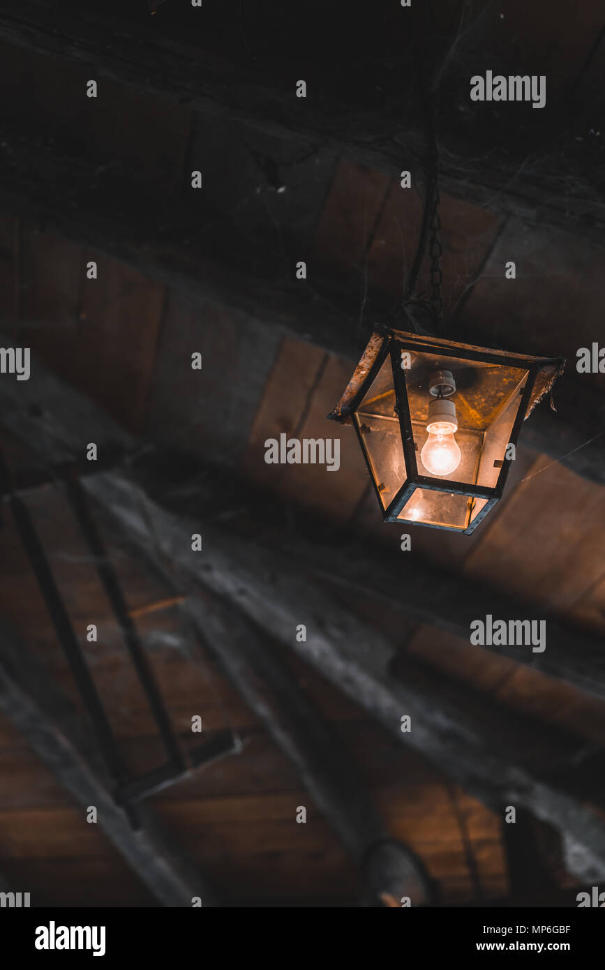 Old lamp covered in spider web hanging from the ceiling in an old farm ...