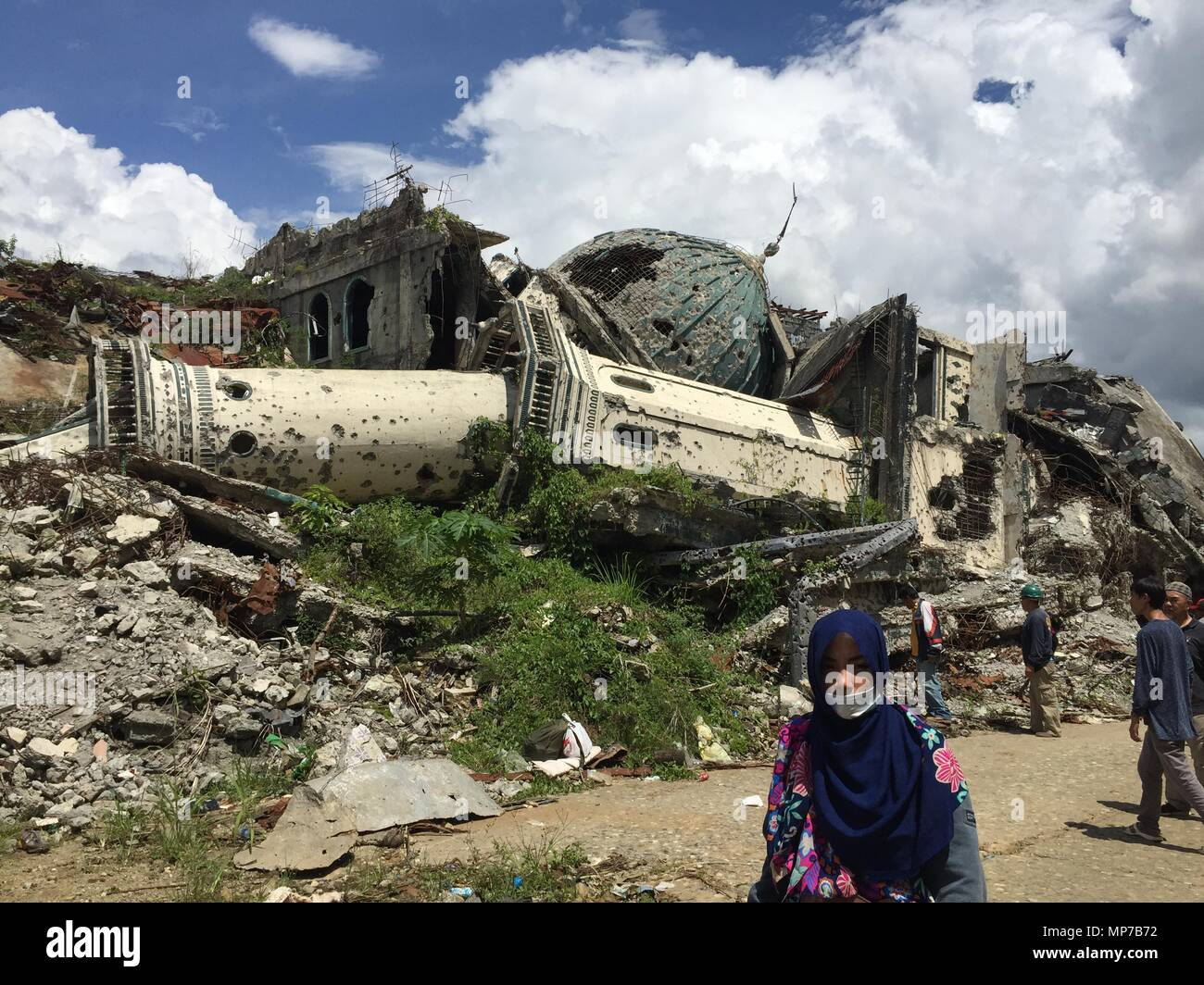 08 May 2018, Philippines, Marawi: A woman walks in front of a toppled ...