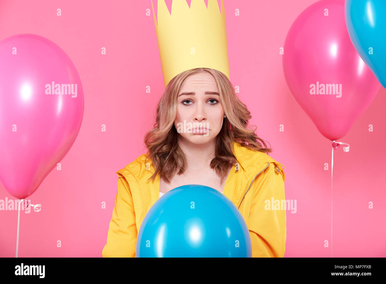 Disappointed young woman in party hat surrounded by colorful balloons ...