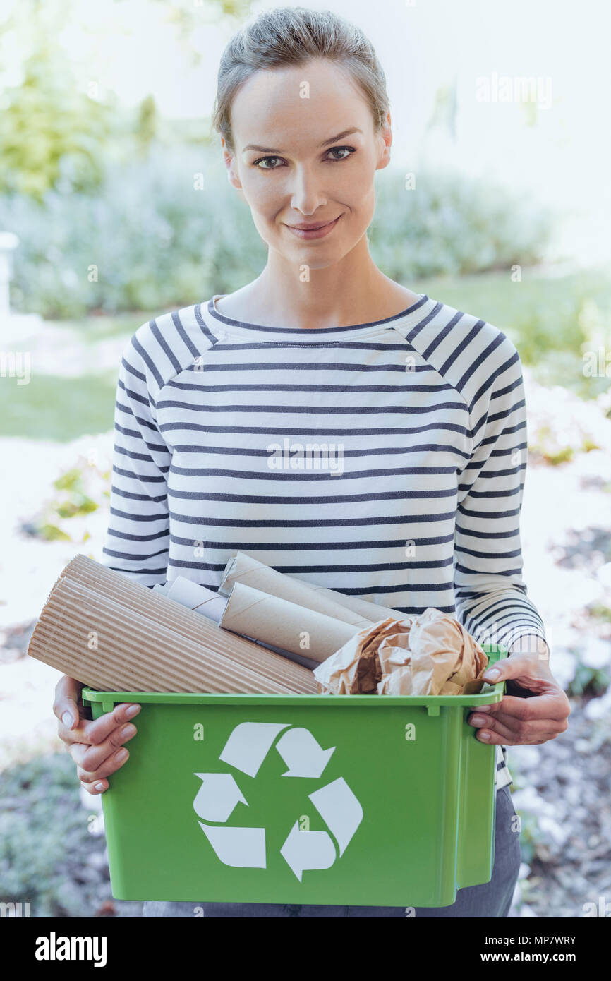 Smiling aware woman holding a green container with segregated paper ...