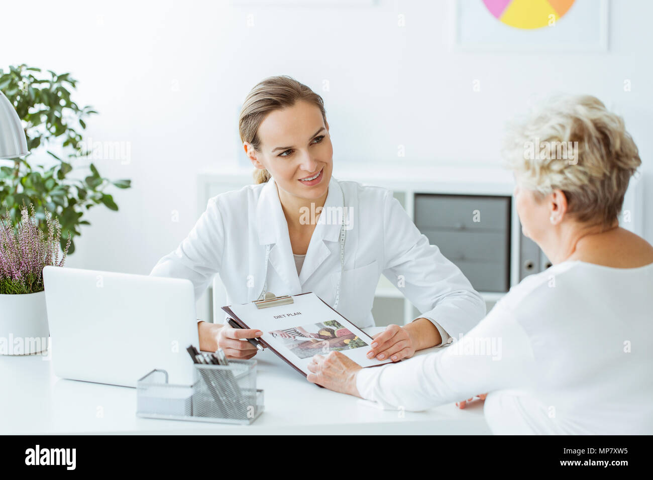 Smiling dietitian holding a diet plan during consultation with patient ...