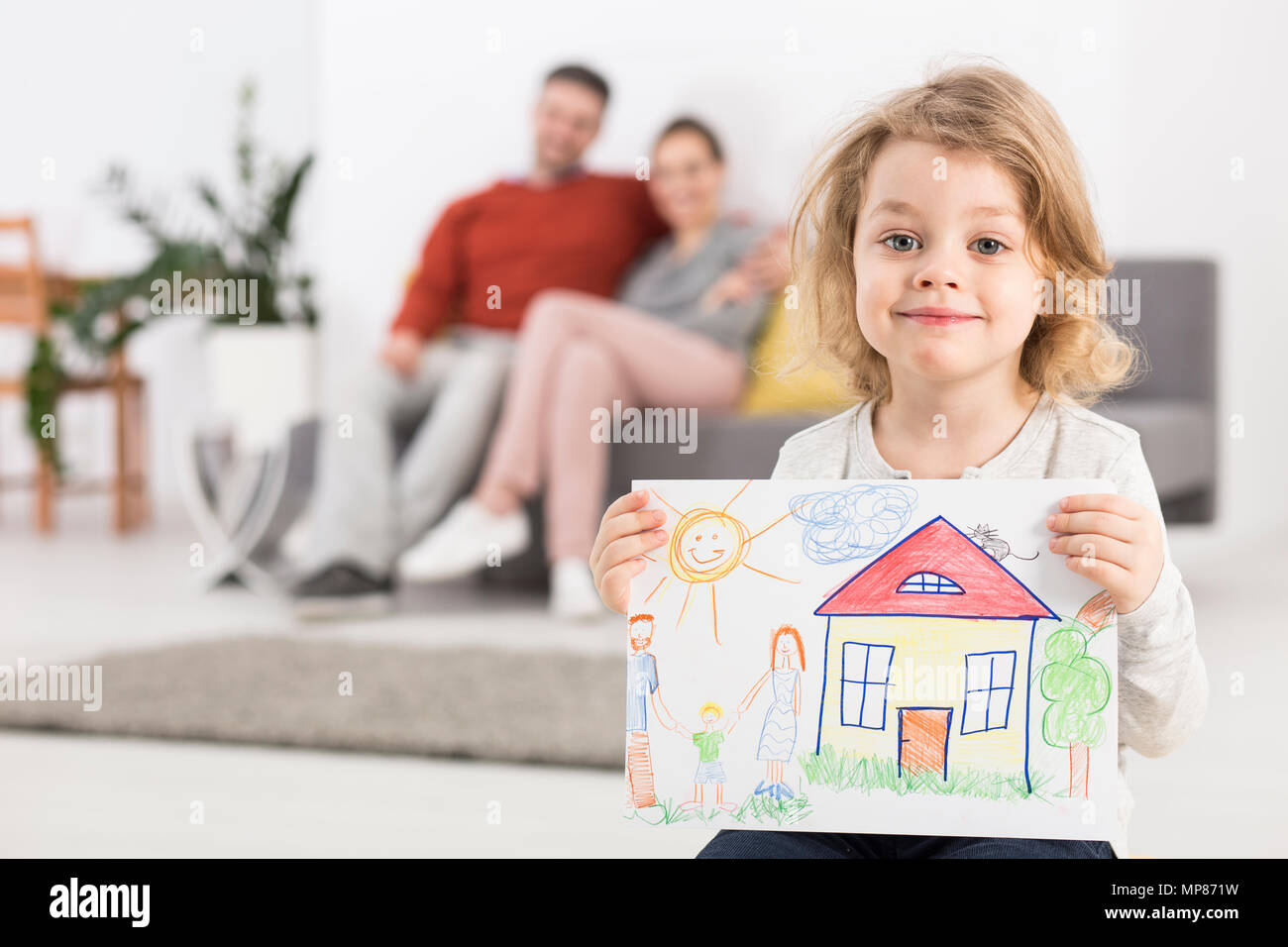 Photo of a smiling little girl holding a drawing with a house, with her ...
