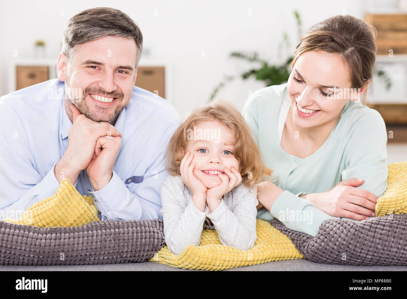 Portrait of a young, happy family lying on a sofa, with a little blonde ...