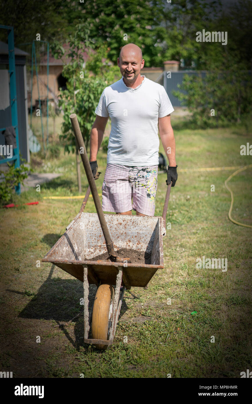 man pushing wheelbarrow. Young man pushing a wheelbarrow on the farm ...