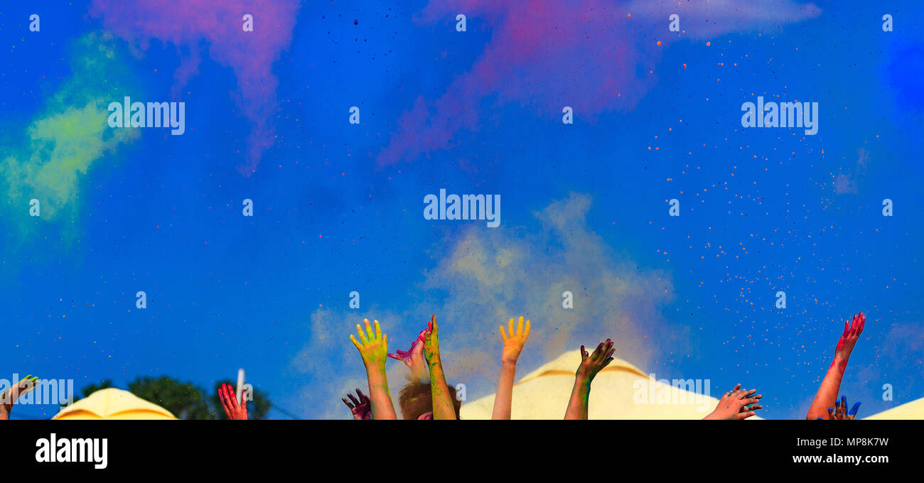 At the color Holi festival, hands in the air, blue sky behind Stock ...