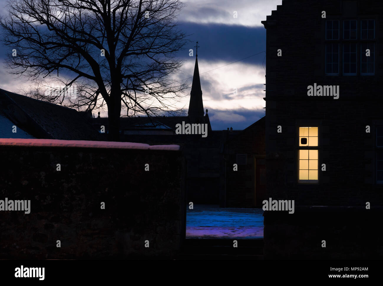 Evening with a church spire, bare tree and lit window in winter Stock ...