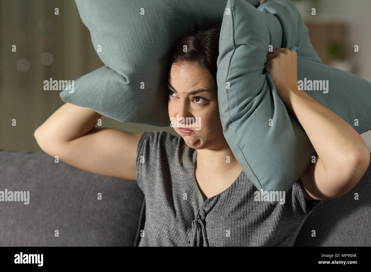 Angry woman suffering neighbour noise sitting on a couch in the living ...