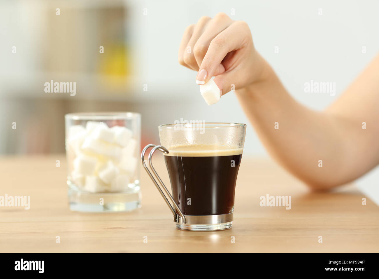 Close up of a woman hand throwing sugar cube into a coffee mug on a ...