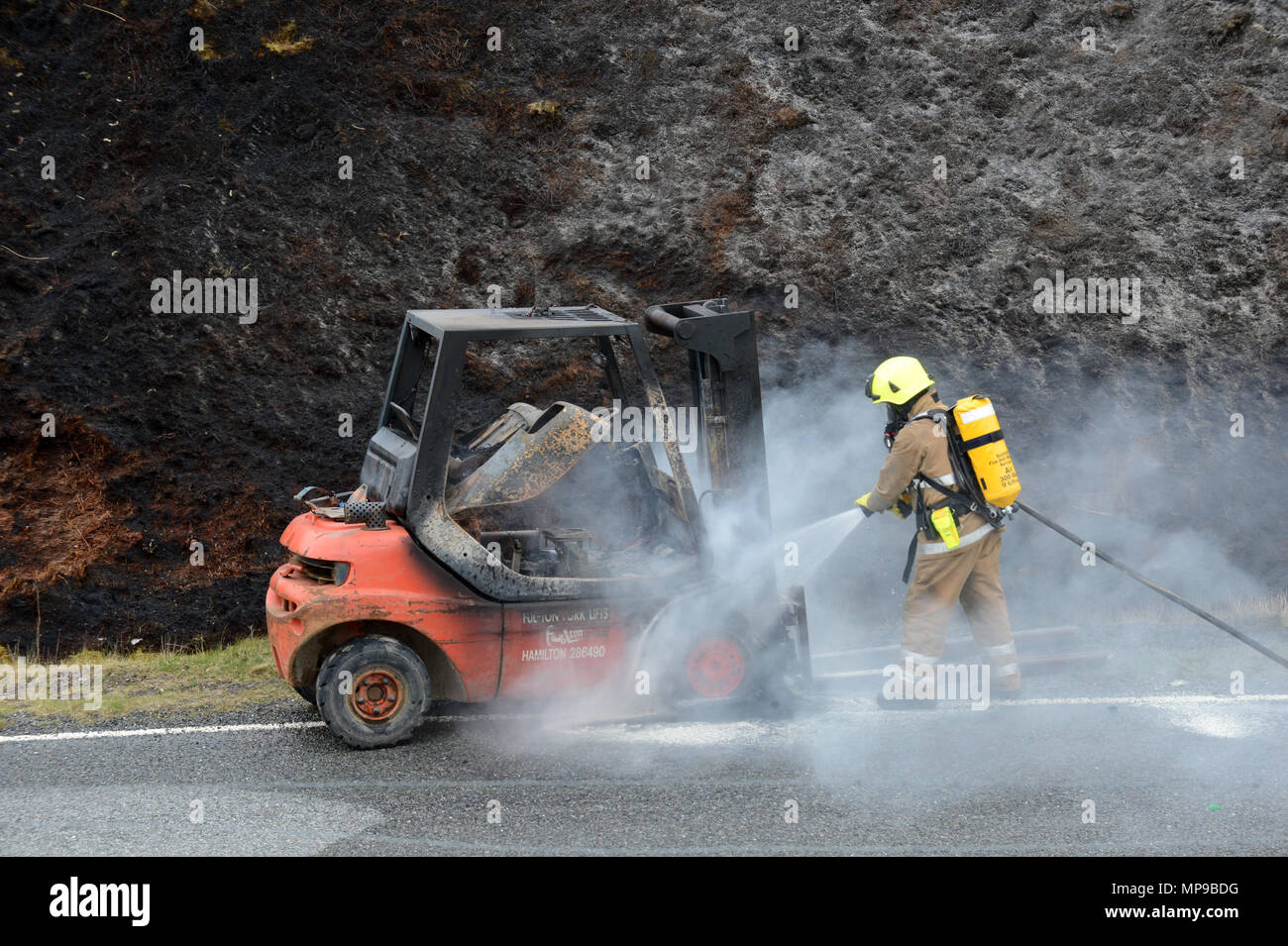 Fireman with breathing apparatus putting out a fire on a main road of a ...