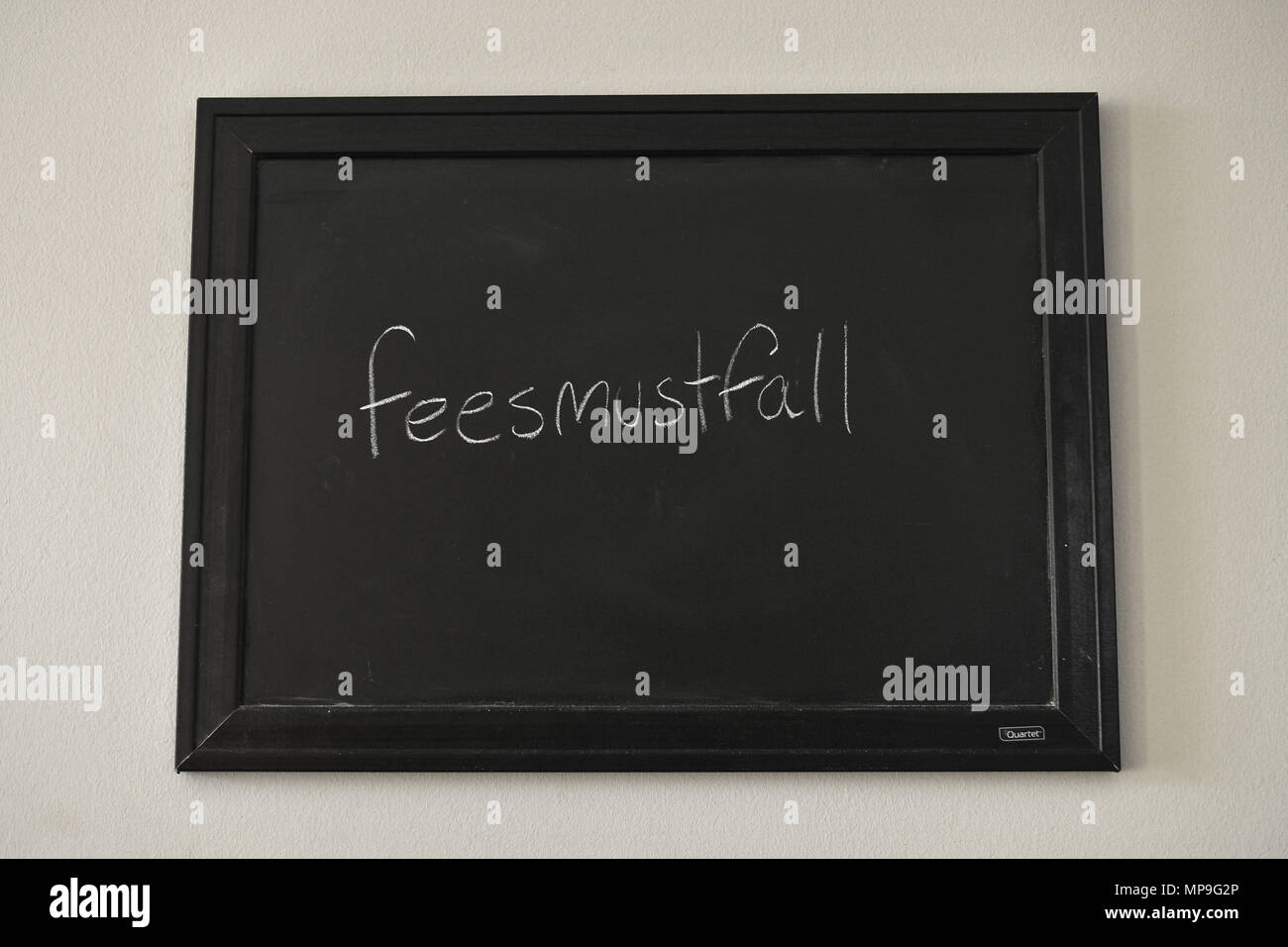 Fees Must Fall written in white chalk on a wall mounted blackboard ...