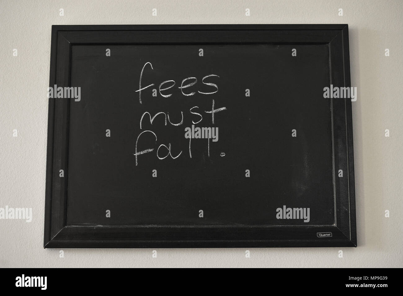 Fees Must Fall written in white chalk on a wall mounted blackboard ...