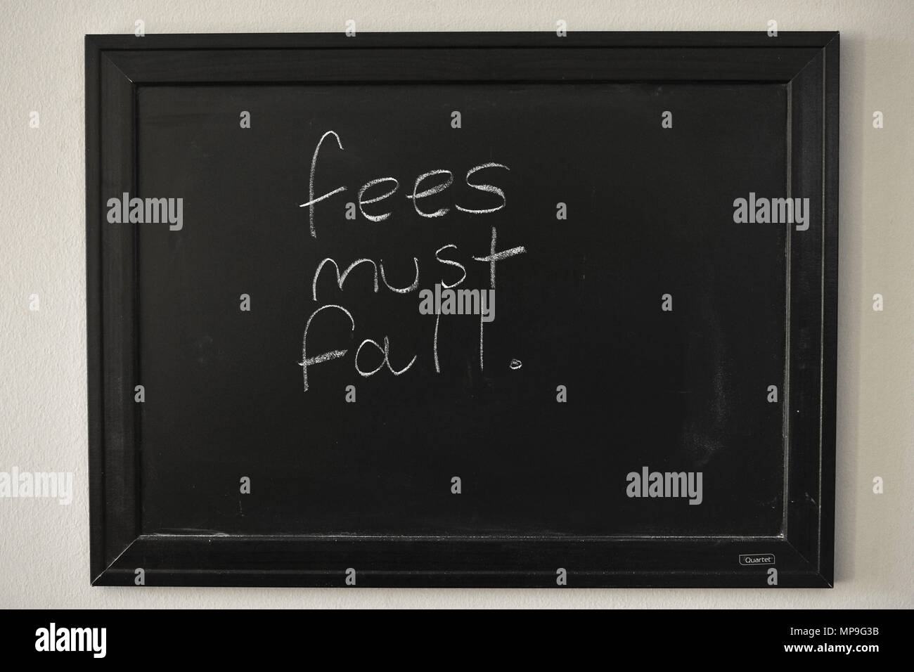 Fees Must Fall written in white chalk on a wall mounted blackboard ...