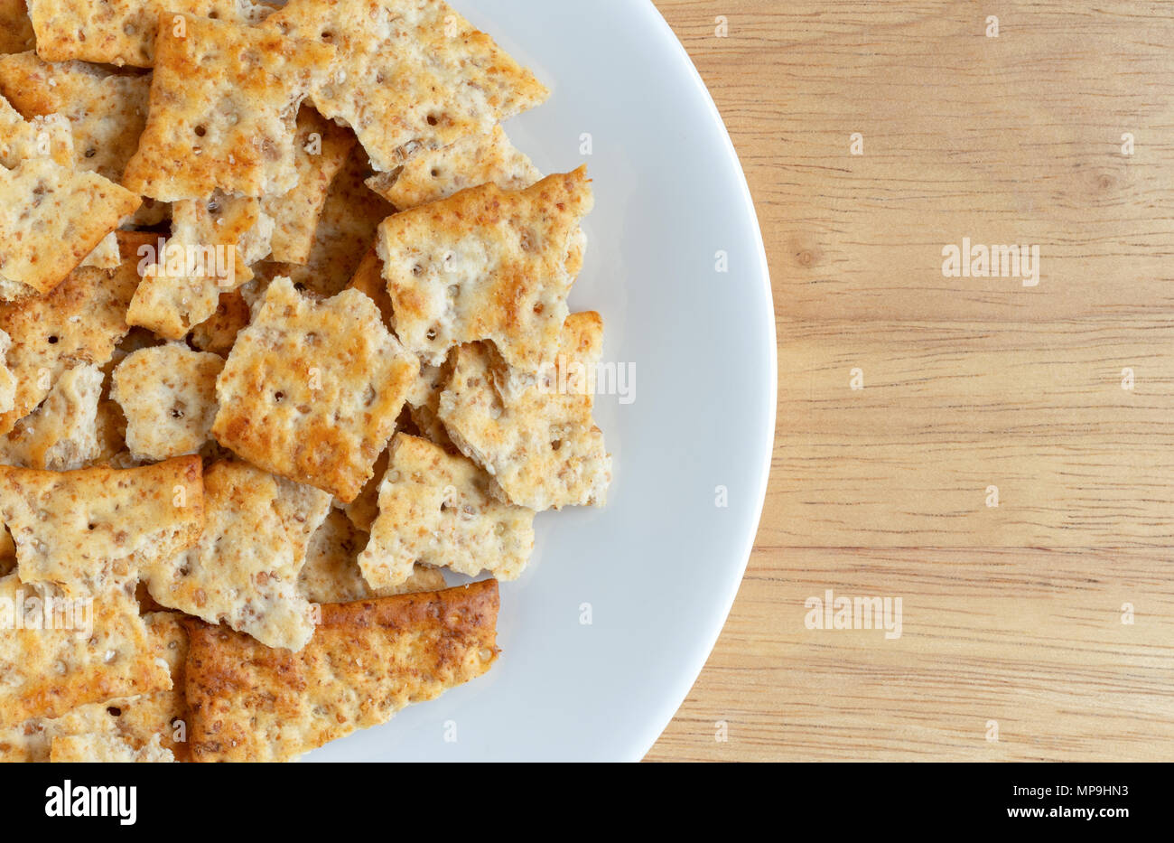 Top close view of a white plate filled with broken multigrain flatbread crackers on a wood ...