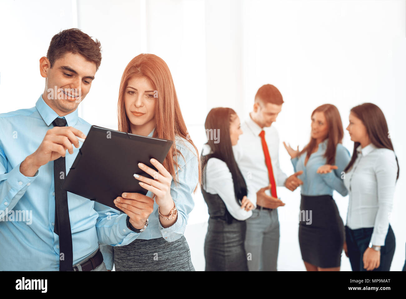 Two smiling young colleagues discussing in front their business team ...