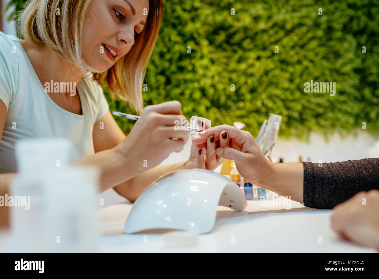 Happy beautician paint the nails of female clients at the beauty salon ...