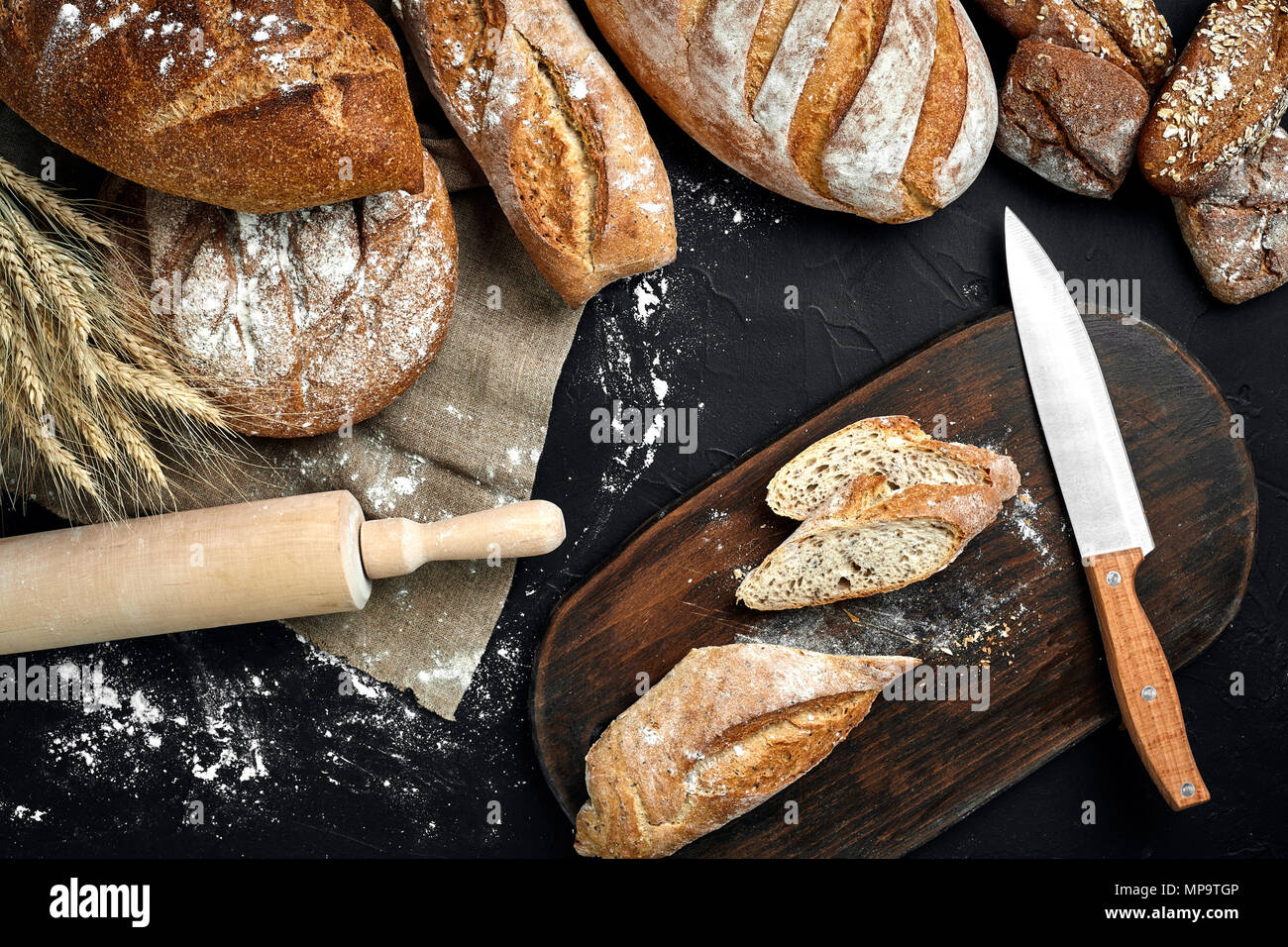 Fresh bread, wooden board and cutting knife on black table Stock Photo ...