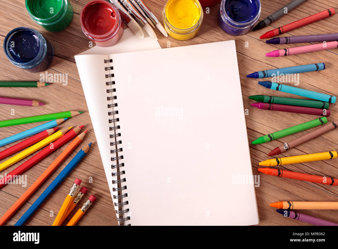 Blank white folded open notebook on a school desk with various paints ...