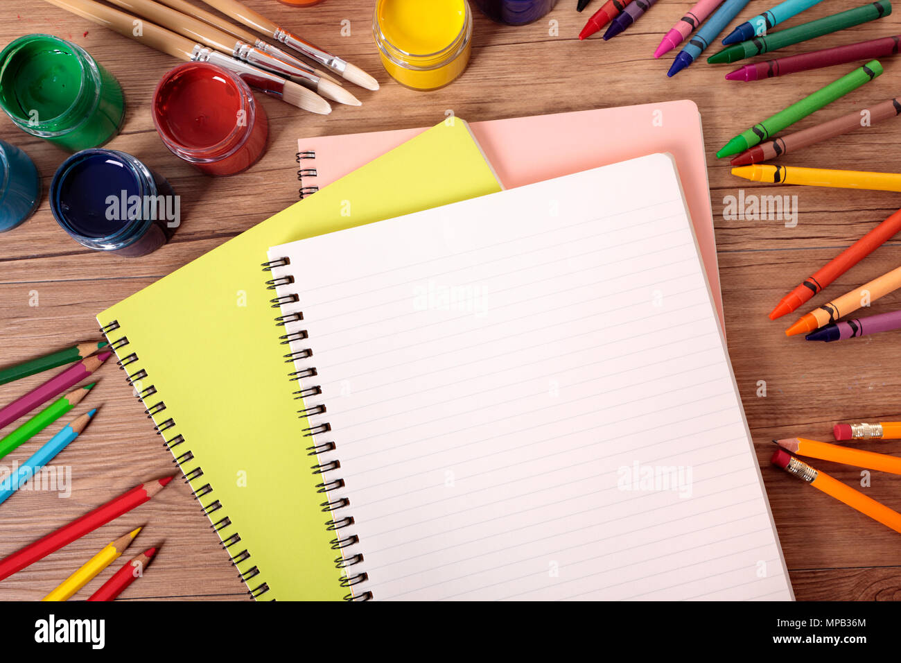 Blank white open notebook on a school desk with various paints, pencils ...