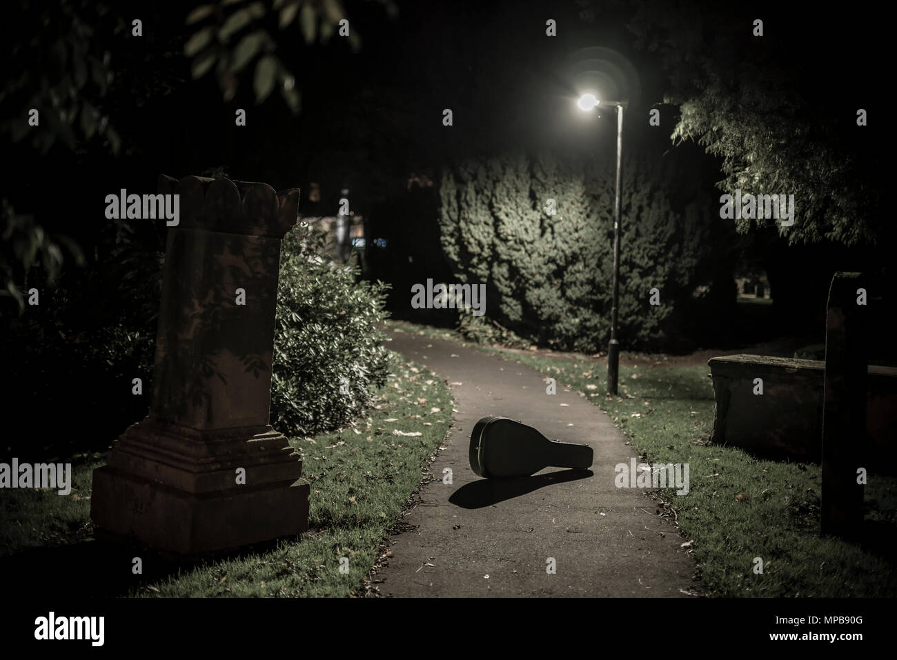 In Kelso churchyard, Scotland. At night. A guitar case by lamplight ...