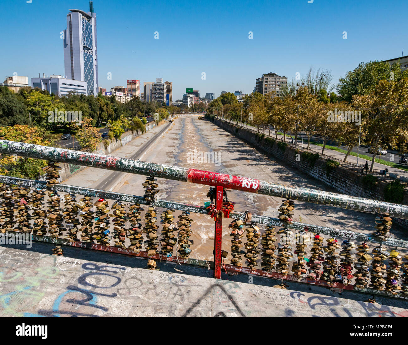 Arched pedestrian bridge over low River Mapocho with mass of love locks ...