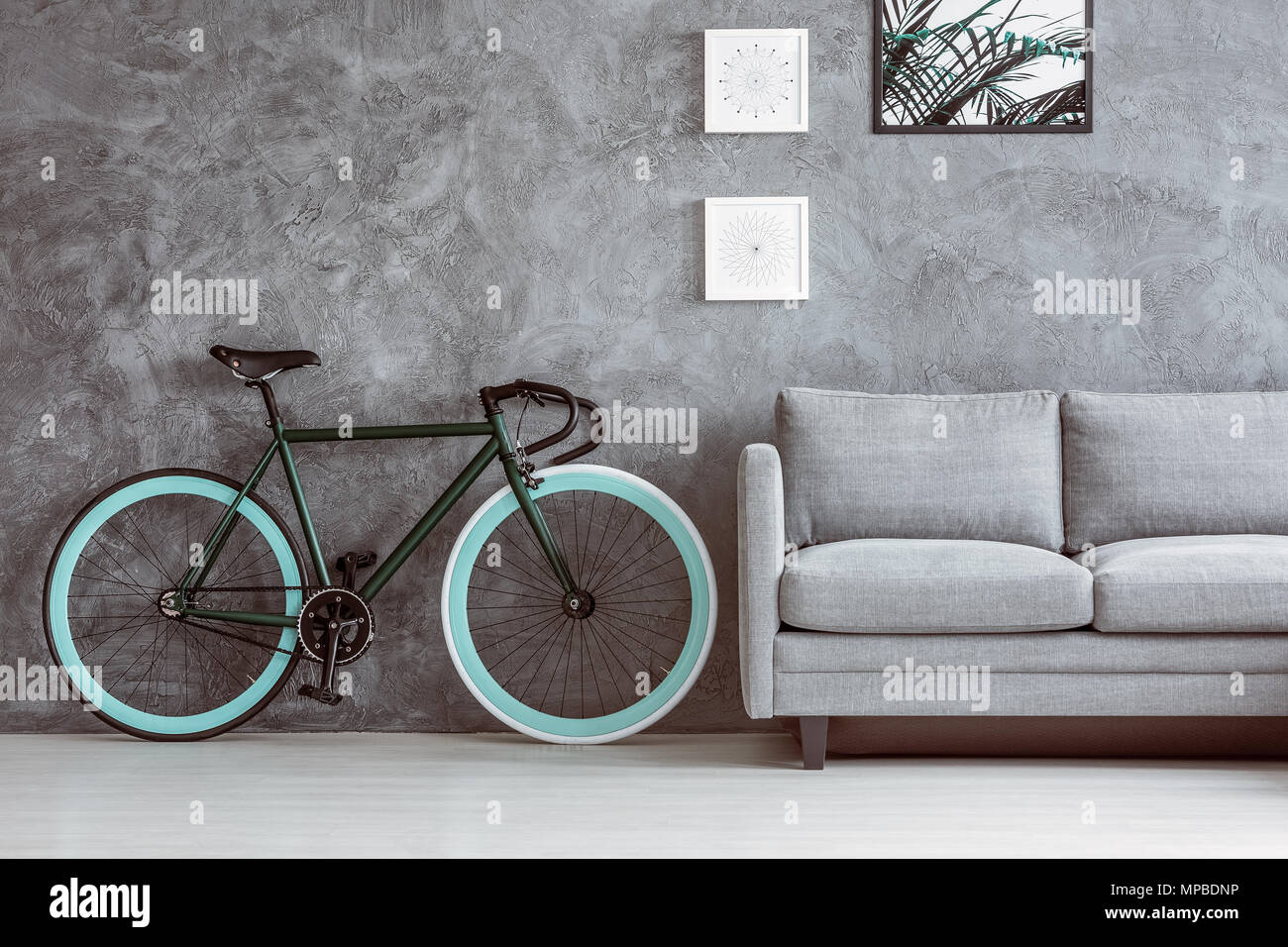 Bike with blue wheels next to grey sofa in living room with posters on ...