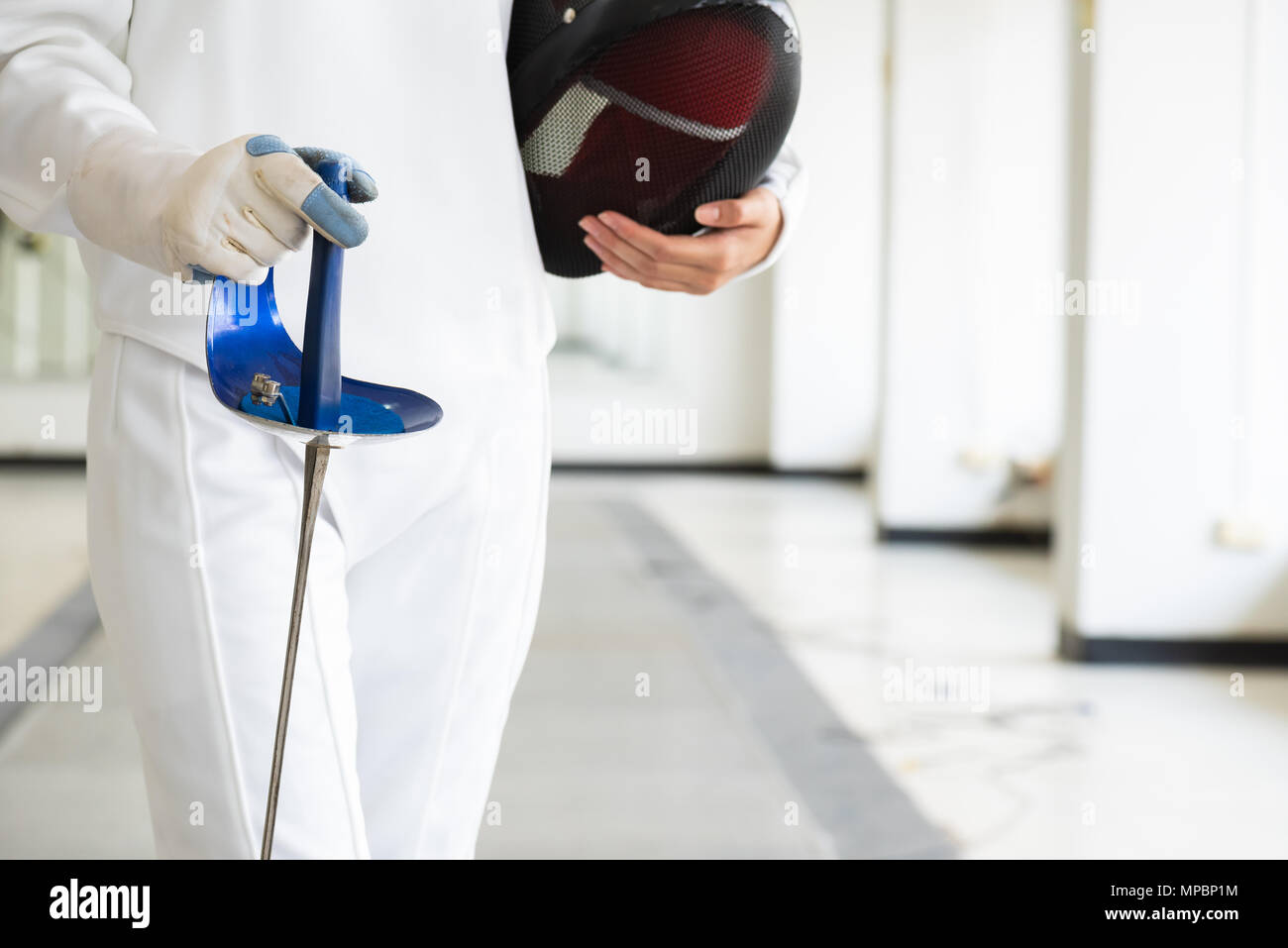 Close-up of a fencer in white fencing suit and holding her mask and a sword. Sport and ...
