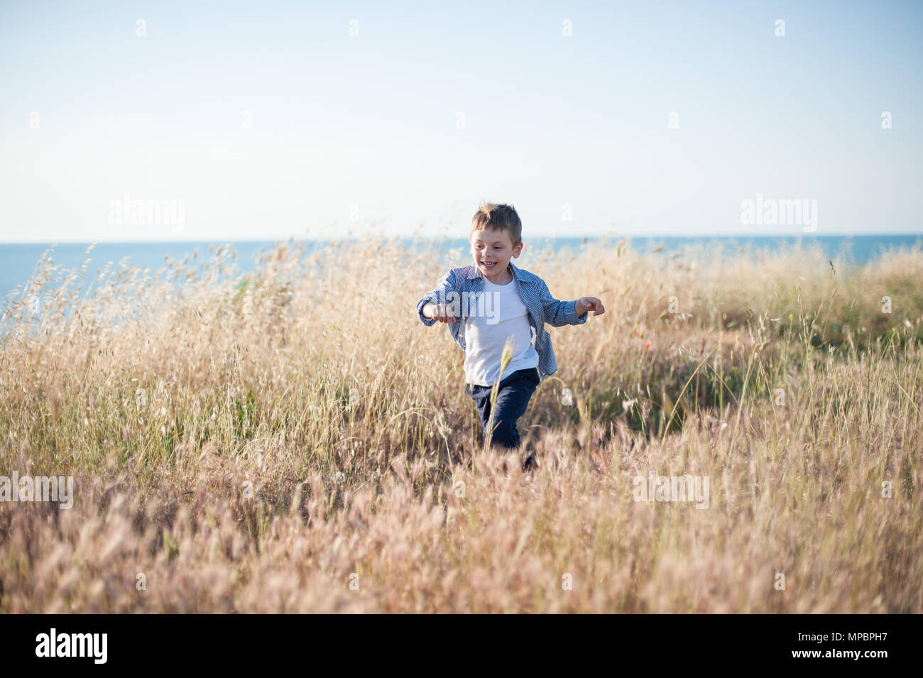 happy smiling little kid running among yellow grass on sea background ...